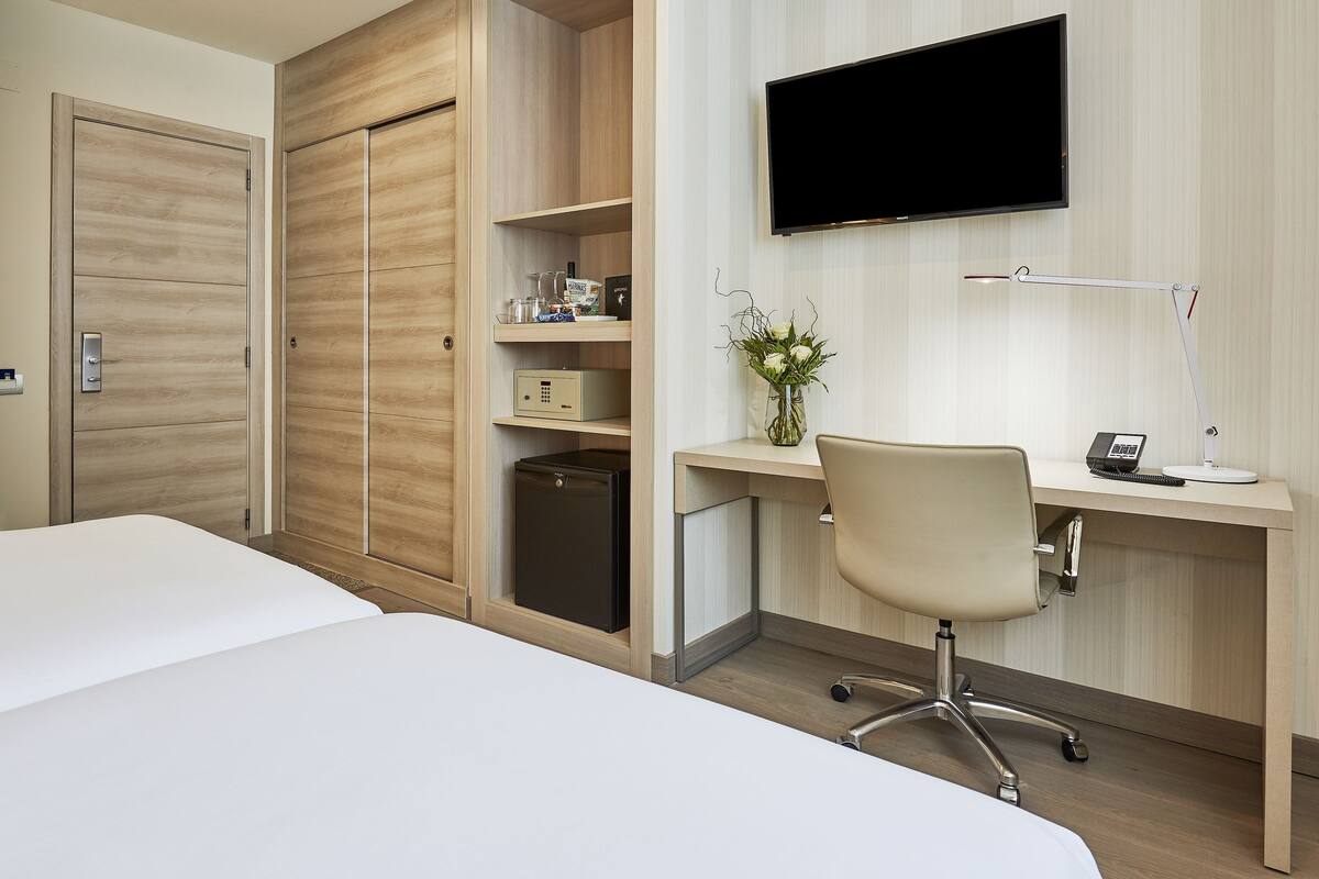 Quarto de hotel com cama, secretária com cadeira, televisão, cofre e minibar.