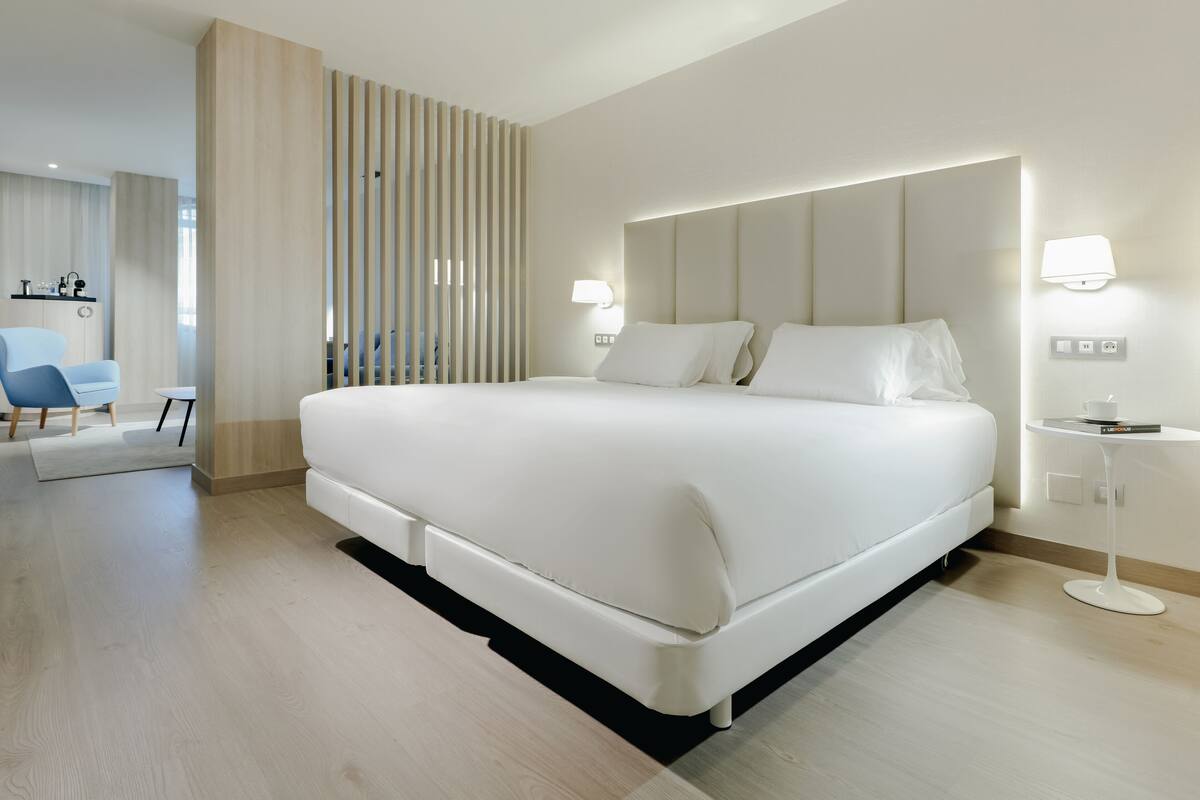 Quarto de hotel moderno com uma cama grande, mesas de cabeceira, uma escrivaninha e uma cadeira.