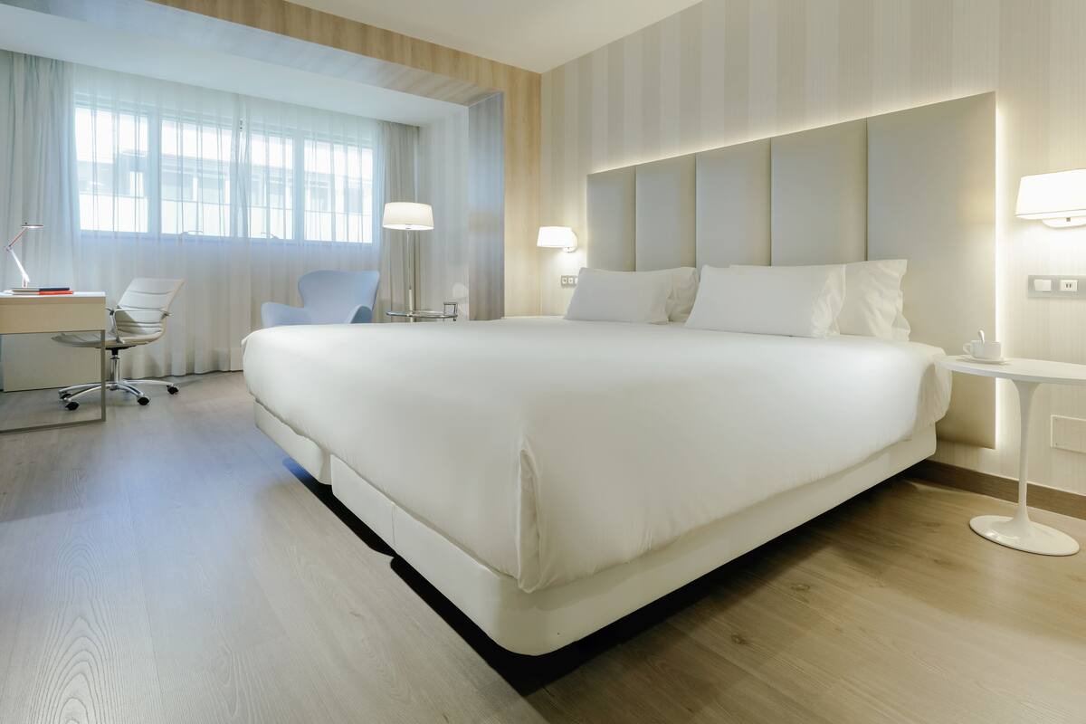 Quarto de hotel moderno com uma cama grande, uma escrivaninha com cadeira e uma pequena mesa com uma chávena.