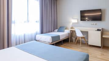 Quarto de hotel com cama, escrivaninha com cadeira, televisão e janela com cortinas.