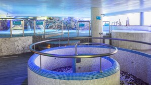 Uma área de spa com uma banheira de hidromassagem circular, uma parede de pedra e um chão revestido de azulejos.