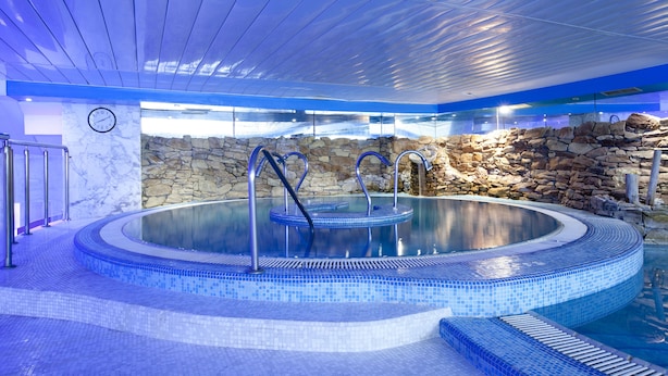 Uma área de spa com parede de pedra, banheira de hidromassagem circular e piso revestido de azulejos.