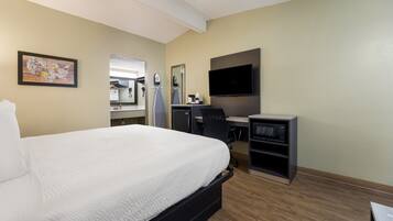 Quarto de hotel com cama, escrivaninha, cadeira, televisão e micro-ondas.