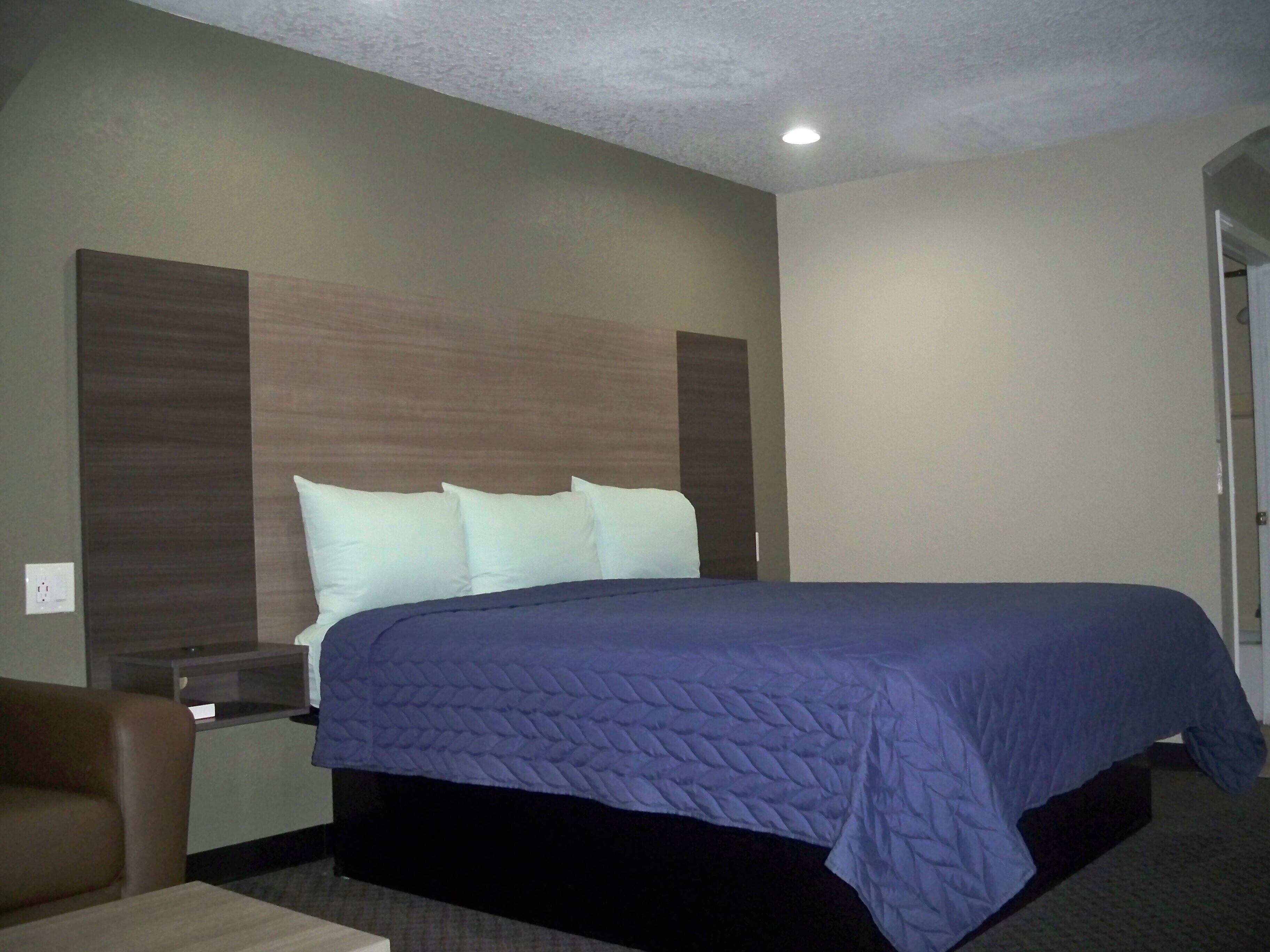 Quarto de hotel com uma cama grande, uma mesa de cabeceira, uma cadeira e um guarda-roupa.