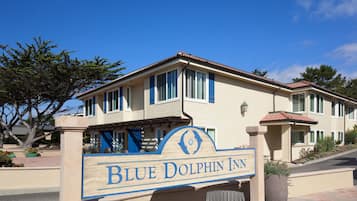Exterior do Blue Dolphin Inn, com placa de identificação, área de estar externa com cadeiras e mesa, e um céu azul claro.