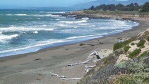 Uma praia costeira com ondas, litoral rochoso e montanhas ao longe.