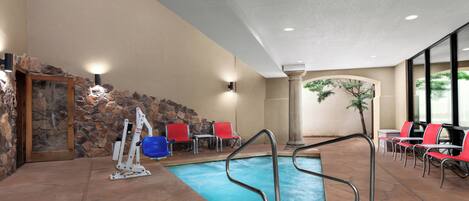 Área de piscina interna com paredes de pedra, cadeiras vermelhas e azuis e um pilar de pedra.