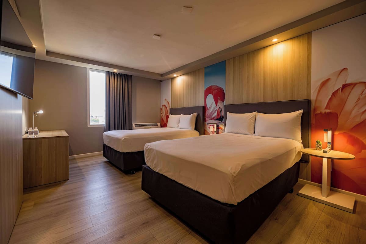 Quarto de hotel com duas camas, mesa de cabeceira com abajur, televisão de tela plana e uma janela grande com cortinas.