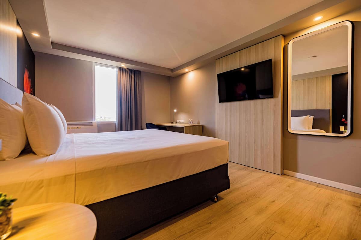 Quarto de hotel moderno com uma cama grande, uma escrivaninha, uma televisão e um espelho.