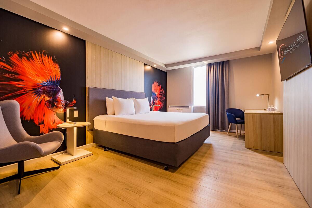Quarto de hotel com cama, escrivaninha, cadeira e uma grande obra de arte na parede.