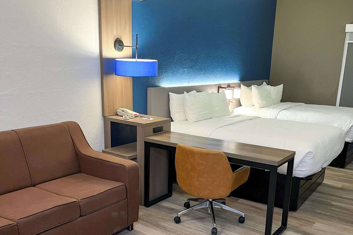 Quarto de hotel com cama, escrivaninha, cadeira, sofá e abajur.