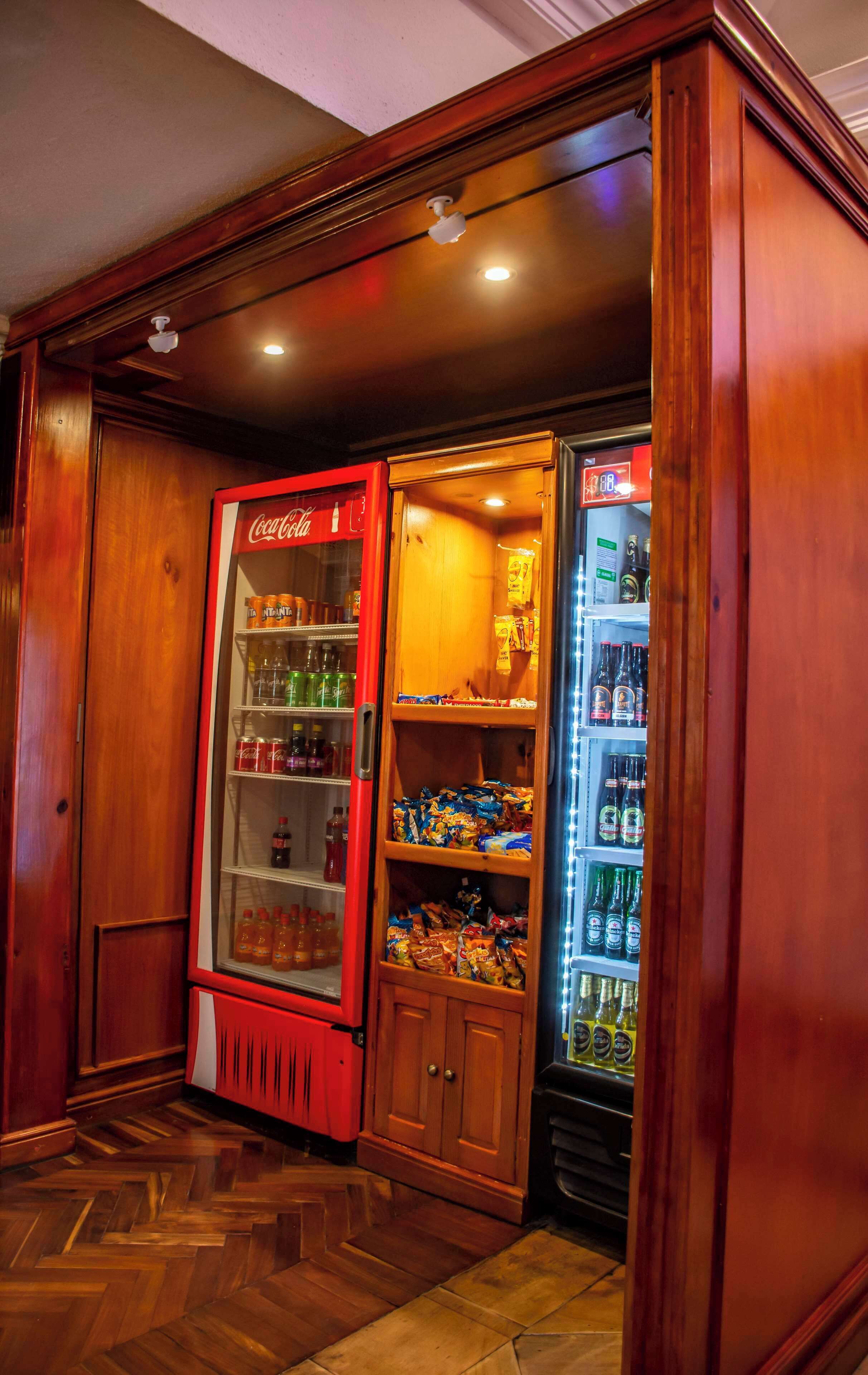 Quarto com piso de madeira, geladeira vermelha Coca-Cola e freezer cheio de bebidas e lanches.
