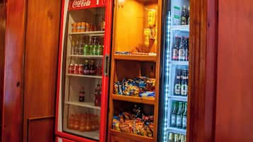 Quarto com piso de madeira, geladeira vermelha Coca-Cola e freezer cheio de bebidas e lanches.