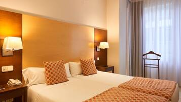 Quarto de hotel com cama de casal, duas luminárias de cabeceira, um telefone e um painel de cabeceira em madeira.