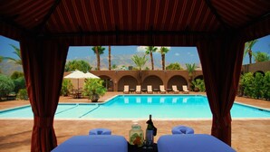 Vista da piscina com área de estar coberta, piscina e montanhas ao fundo.