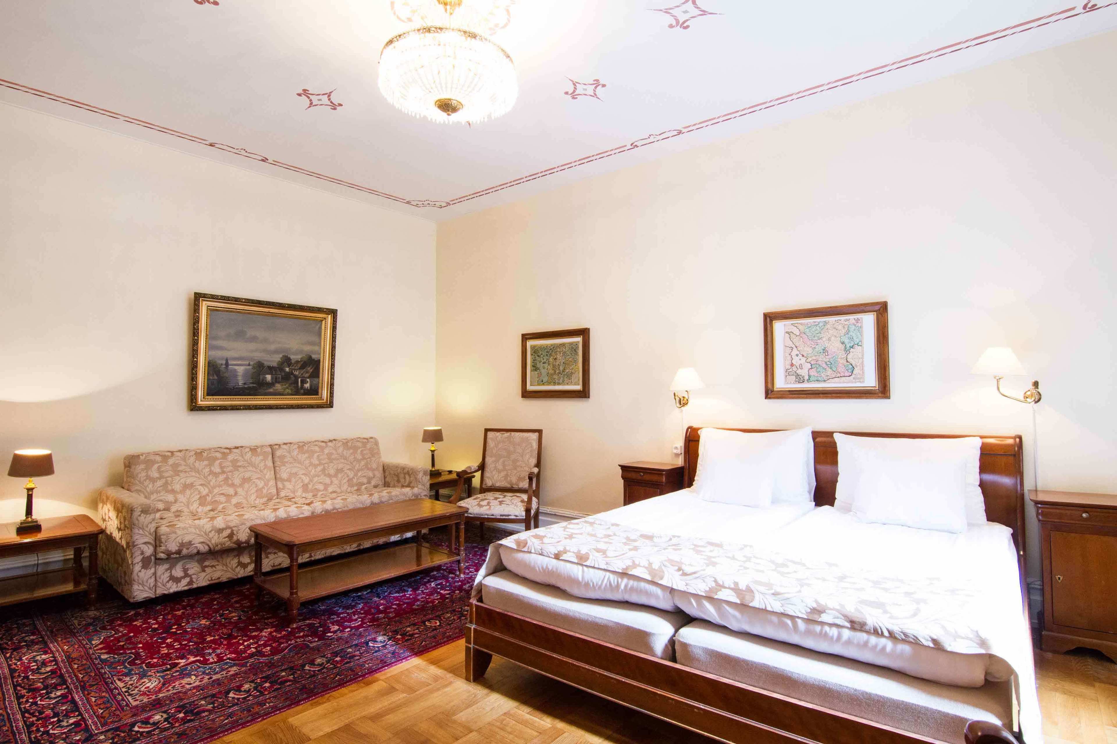 Quarto de hotel com cama, sofá, cadeira, mesa pequena e tapete.