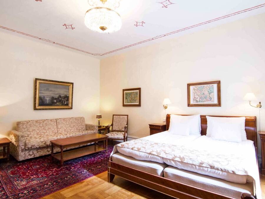 Quarto de hotel com cama, sofá, cadeira, mesa pequena e tapete.