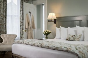 Quarto de hotel com cama, cadeira, abajur e um vaso com flores.