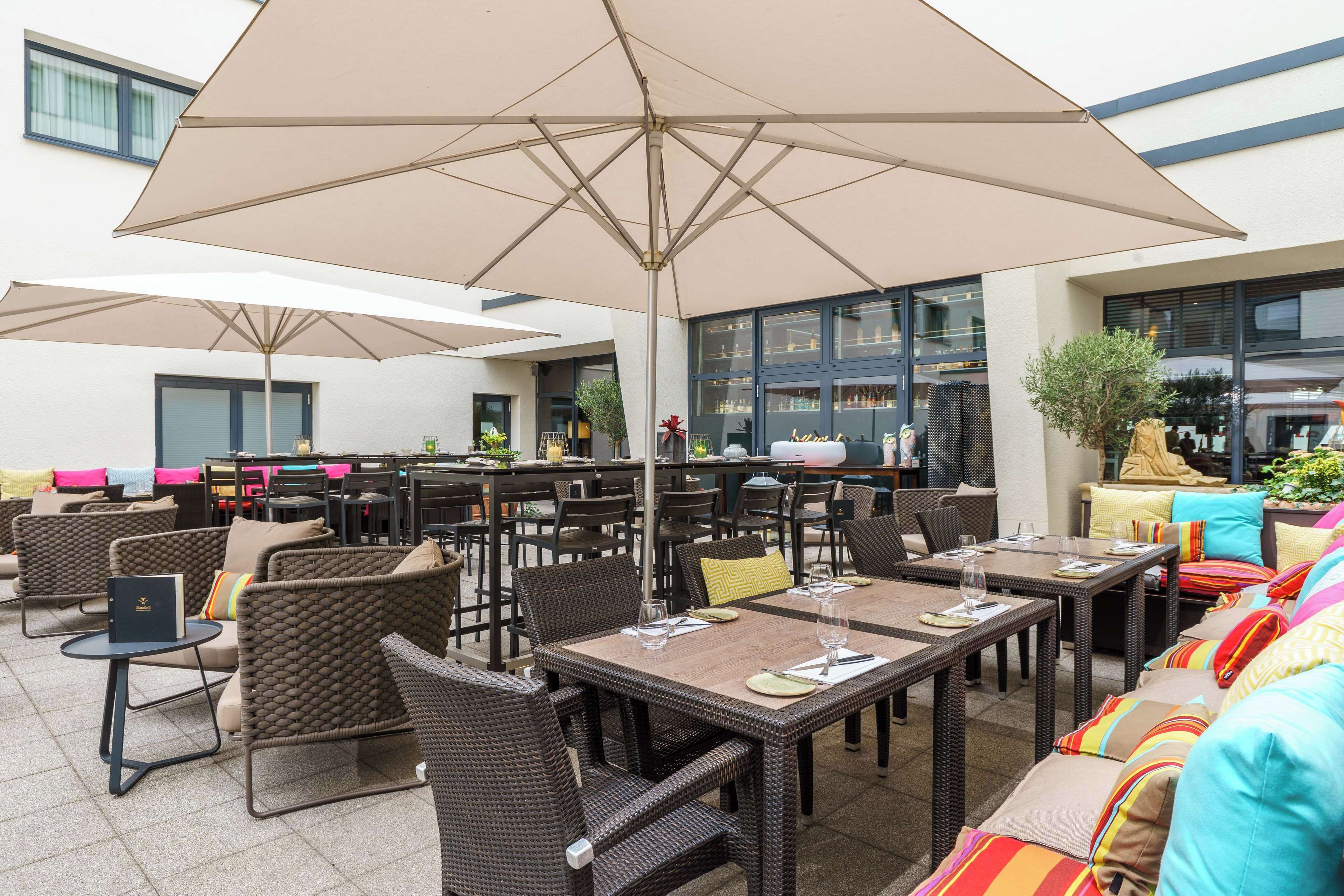 Uma área de refeições ao ar livre com móveis de vime, grandes guarda-sóis e vista para o restaurante.