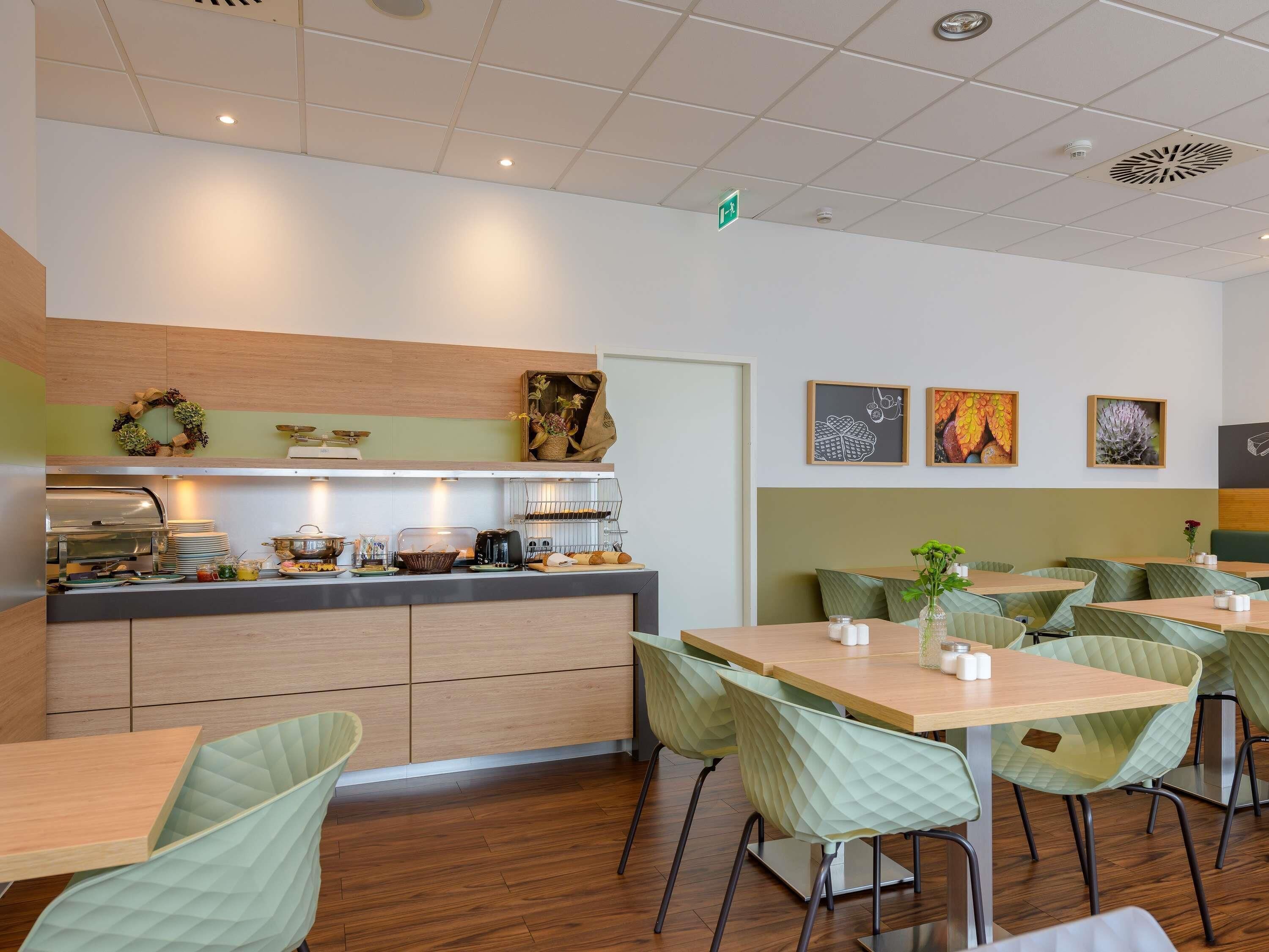 Uma área de refeições moderna com buffet, cadeiras verdes e teto de madeira.