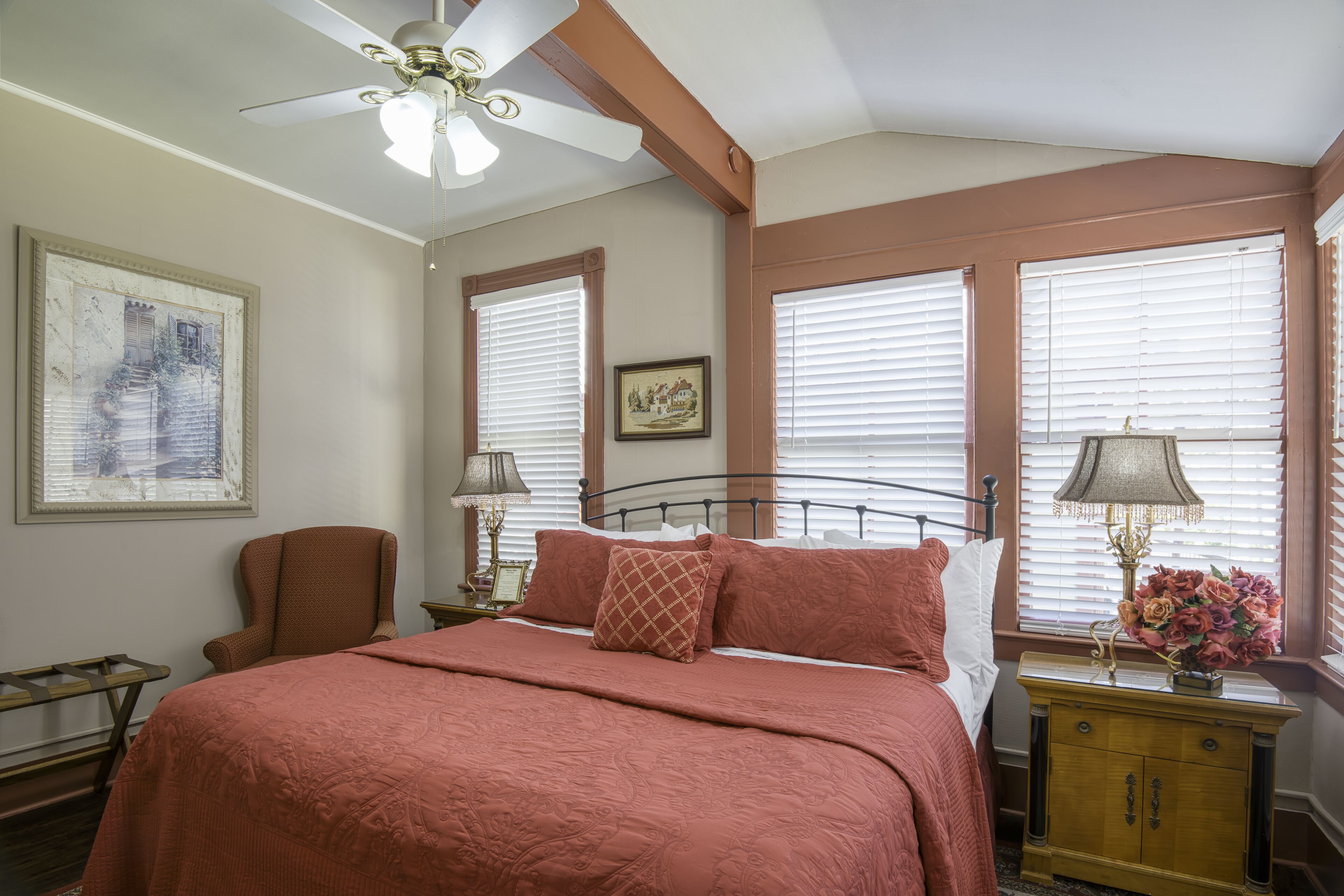 Quarto com cama, cadeira, mesa de cabeceira, luminária e ventilador de teto.