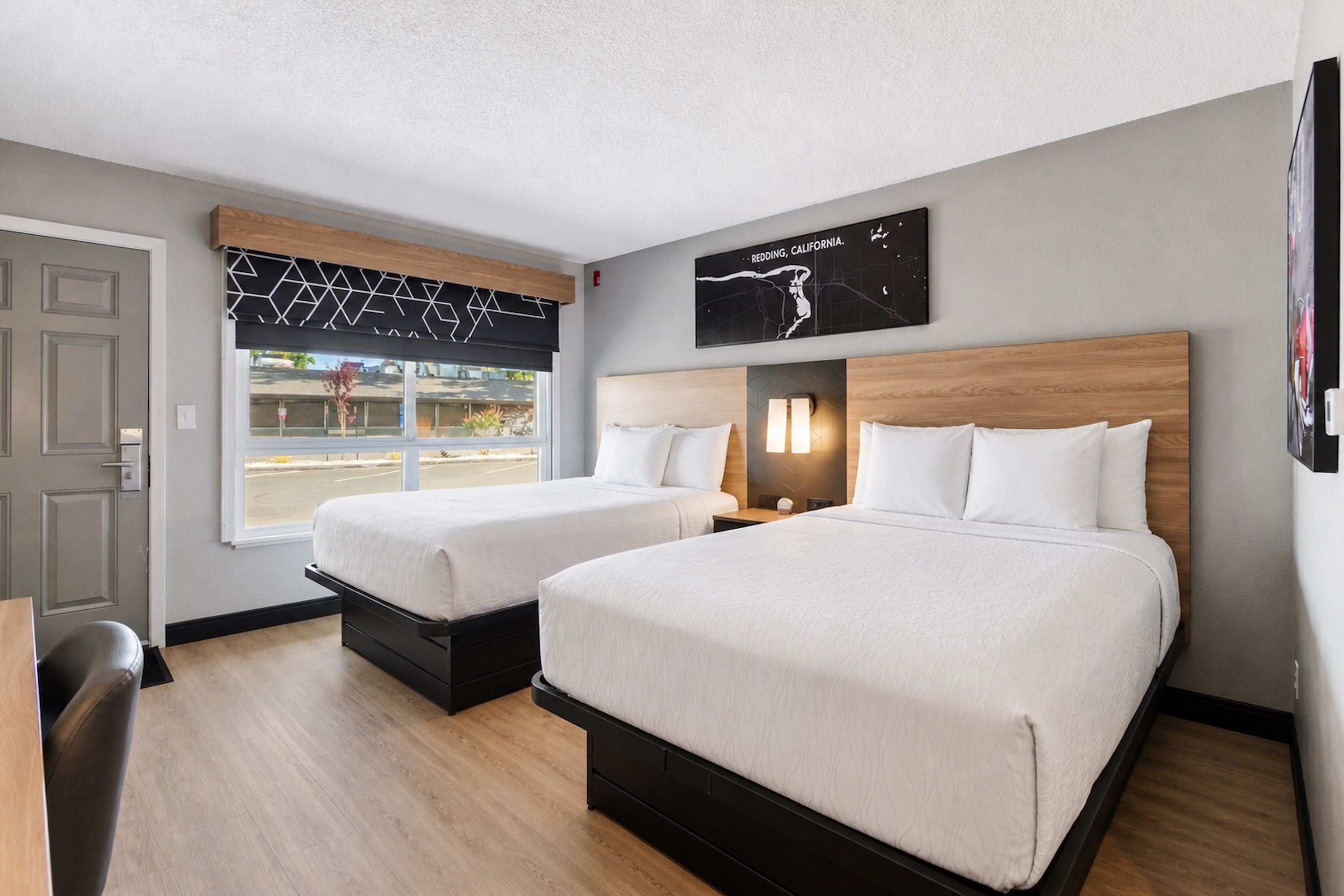Quarto de hotel com duas camas, uma escrivaninha, uma janela com vista e um mapa na parede.