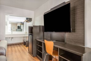 Quarto moderno com televisão de tela plana na parede, piso de madeira e escrivaninha embutida com cadeira.