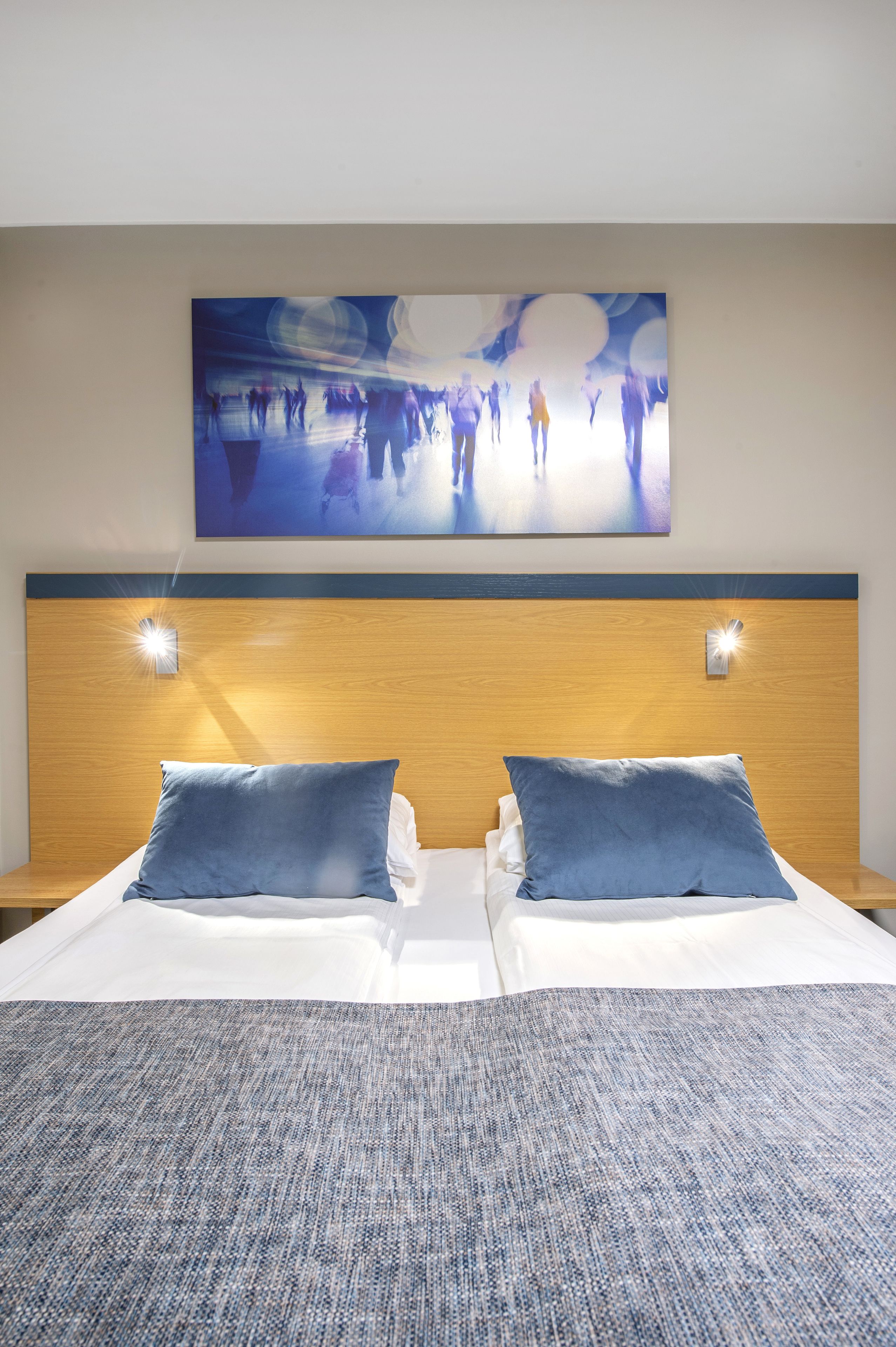 Quarto de hotel com uma cama grande, duas almofadas, cabeceira e um quadro pendurado na parede.