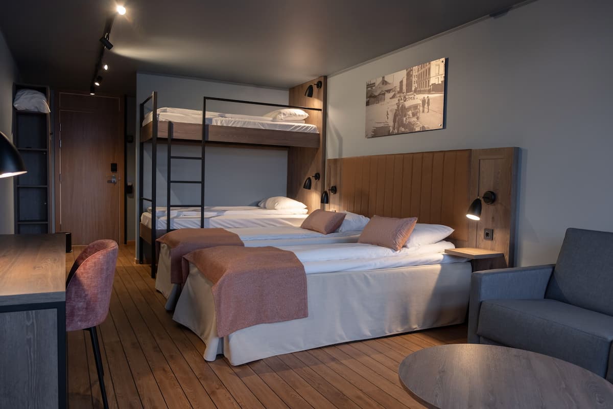 Quarto de hotel moderno com beliches, uma escrivaninha e um sofá.