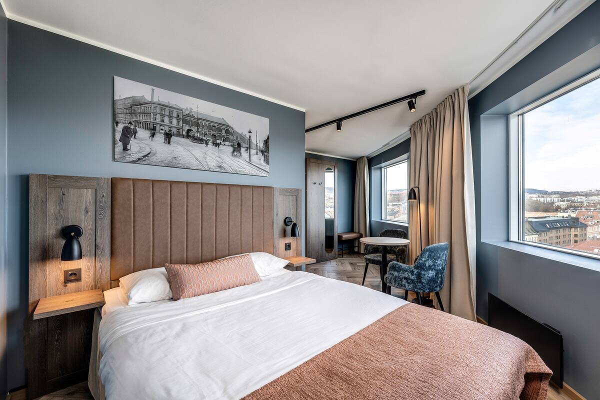 Quarto de hotel moderno com uma cama grande, área de jantar e vista para a cidade.