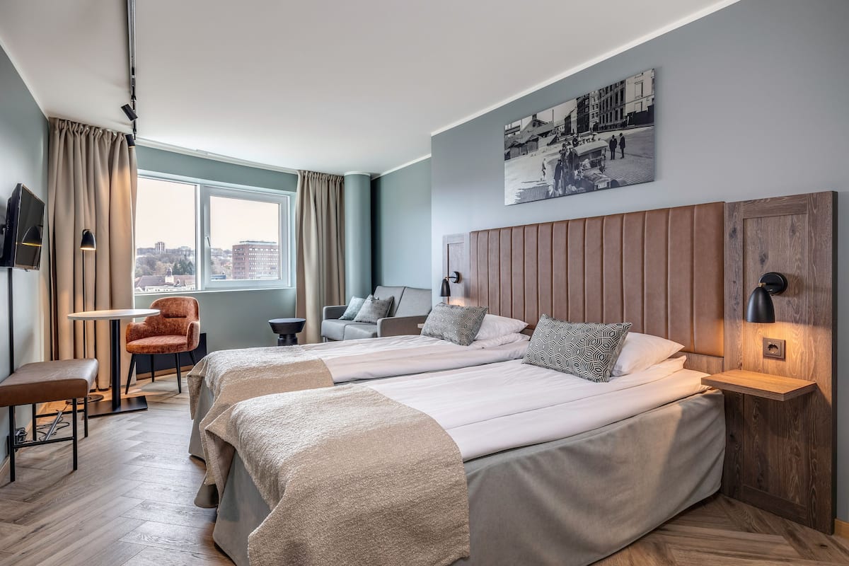Quarto de hotel com duas camas, uma escrivaninha, uma cadeira e vista para a cidade.