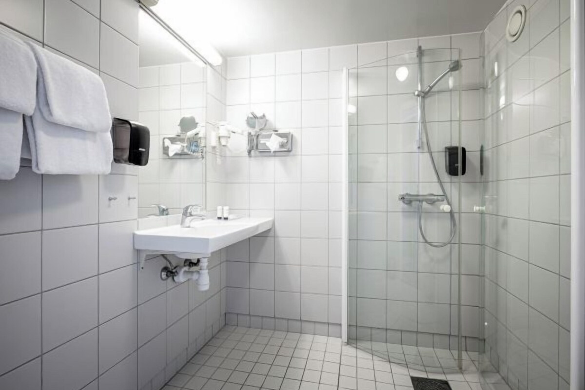 Uma casa de banho moderna com chuveiro de vidro, lavatório branco e porta-toalhas.