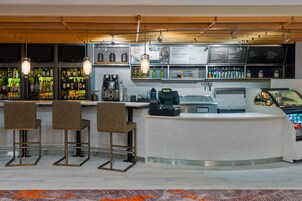 Uma área de bar com balcão, três banquetas, uma máquina de café e um quadro de cardápio.