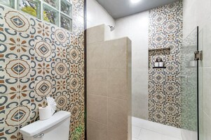 Casa de banho com azulejos estampados, sanita, zona de duche e cabine de vidro.