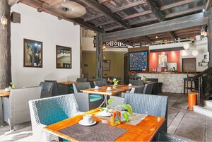 Restaurante com mesas de madeira, cadeiras de vime e um muro de pedra ao fundo.