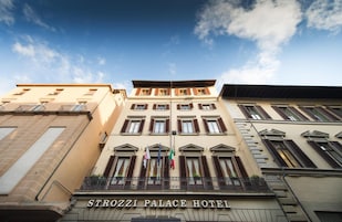 Exterior do Hotel Strozzi Palace, com céu claro e várias bandeiras.