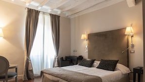 Quarto de hotel com uma cama grande, duas luminárias de cabeceira, uma escrivaninha com cadeira e uma janela com cortinas.
