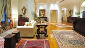 Uma sala de estar ampla com sofá, mesa de centro e lareira. Dois tapetes grandes no chão e um quadro na parede.