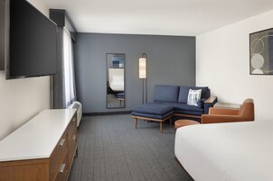 Quarto de hotel com cama, sofá, escrivaninha, espelho e televisão.