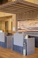 Uma área de recepção de hotel com design moderno, incluindo um balcão de atendimento, uma grande obra de arte abstrata e um candeeiro decorativo.