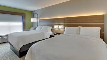 Quarto de hotel com duas camas, uma mesa de cabeceira com abajur e uma janela grande com persianas.