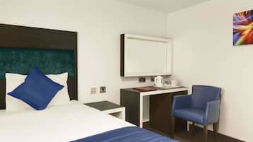 Quarto de hotel com cama, escrivaninha, cadeira, espelho e um quadro na parede.