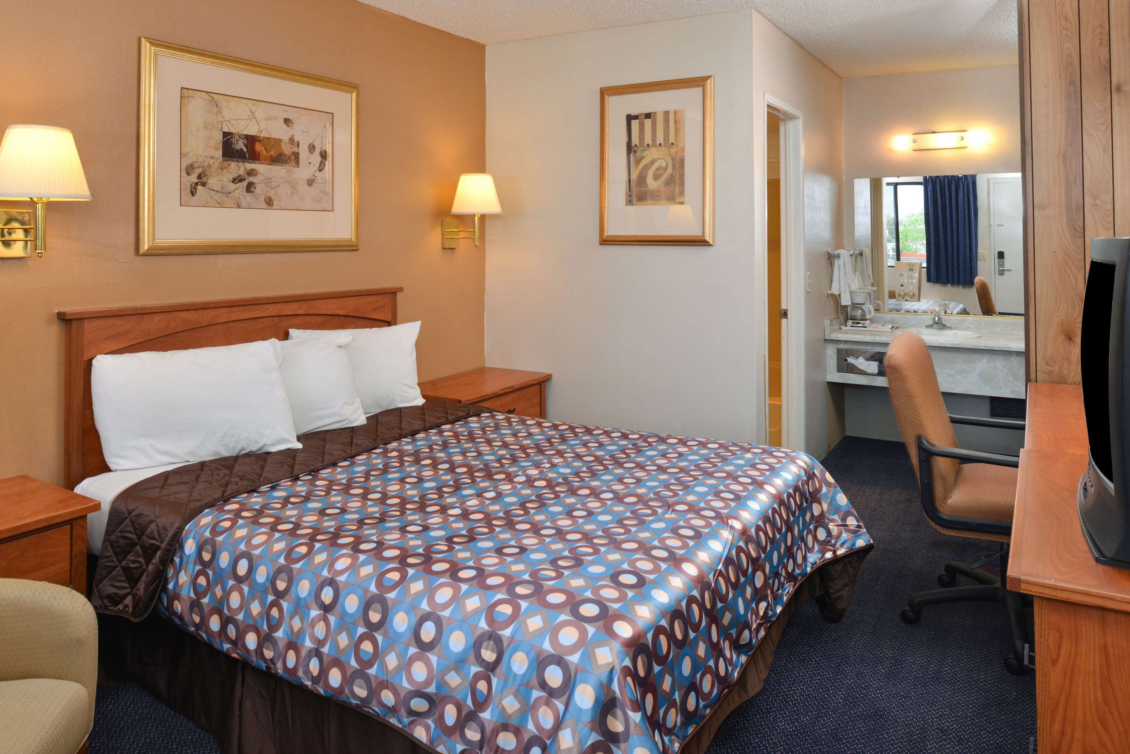 Quarto de hotel com uma cama, uma secretária com cadeira, uma televisão e duas luminárias fixadas na parede.