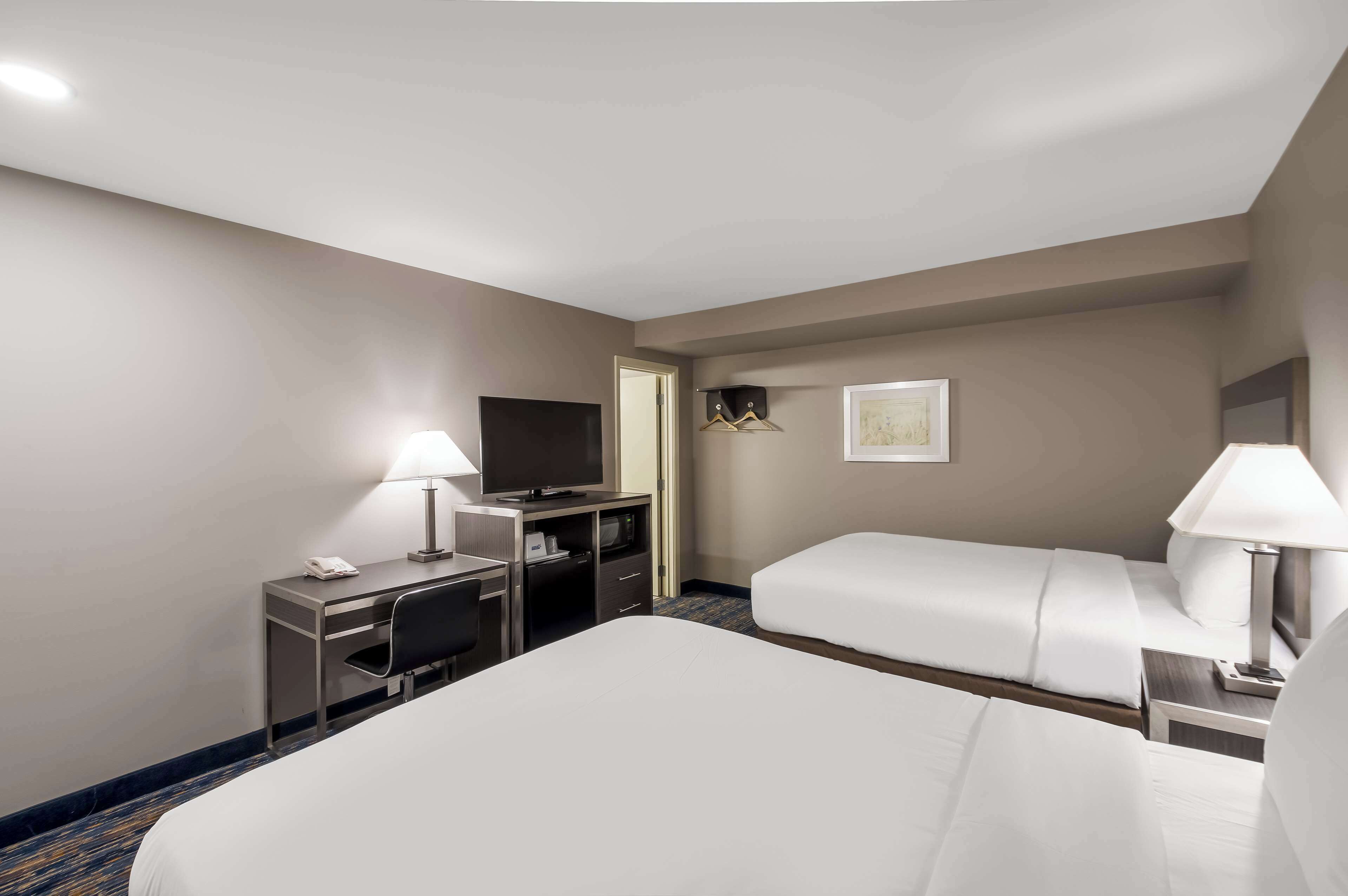 Quarto de hotel com uma cama grande, uma escrivaninha com computador e telefone, uma televisão e duas luminárias de cabeceira.