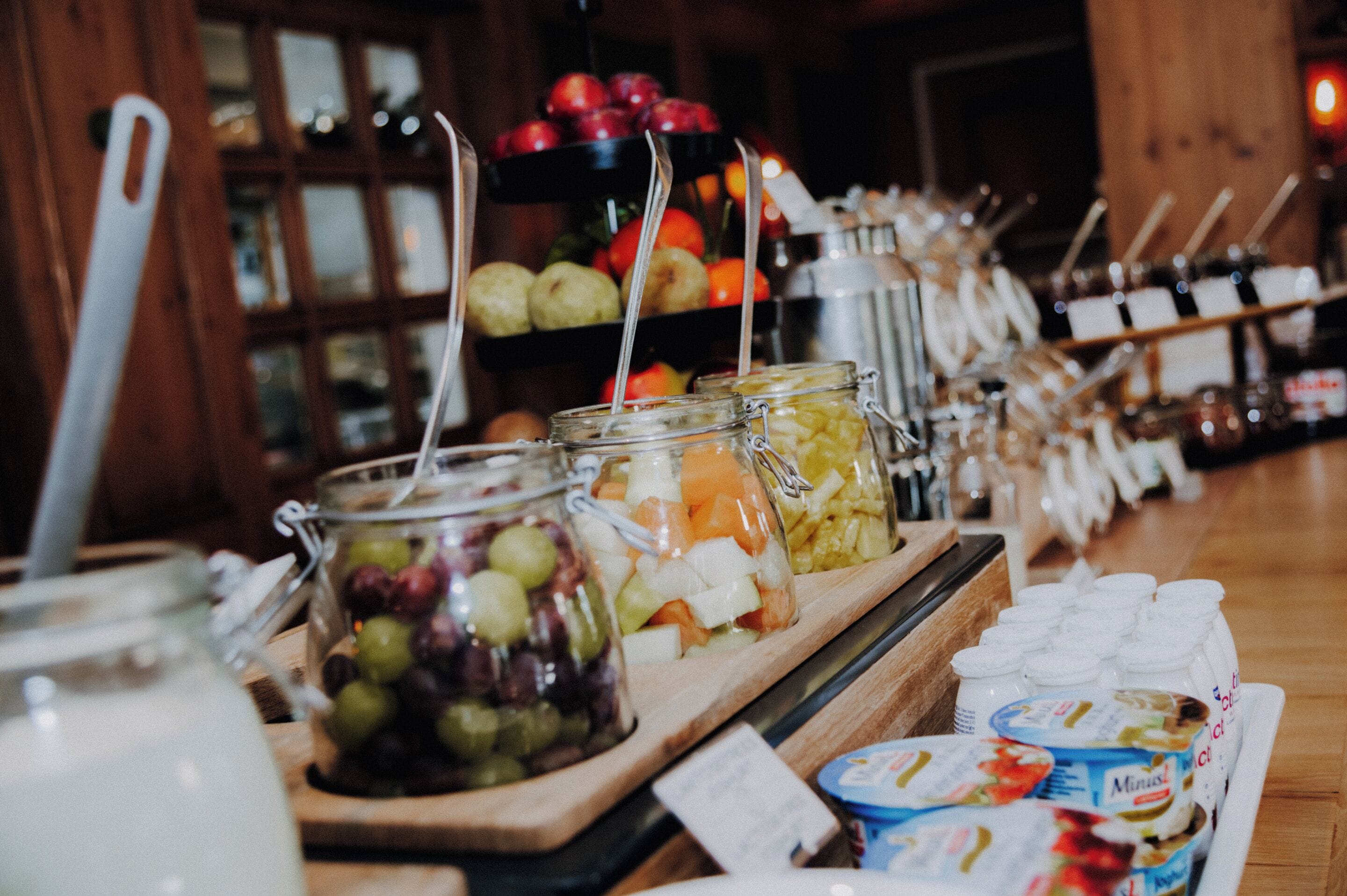 Buffet com diversos alimentos, incluindo potes de picles, queijos e frutas.