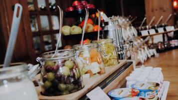 Buffet com diversos alimentos, incluindo potes de picles, queijos e frutas.
