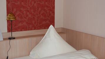 Cama bem arrumada com travesseiro branco e abajur sobre um criado-mudo de madeira.