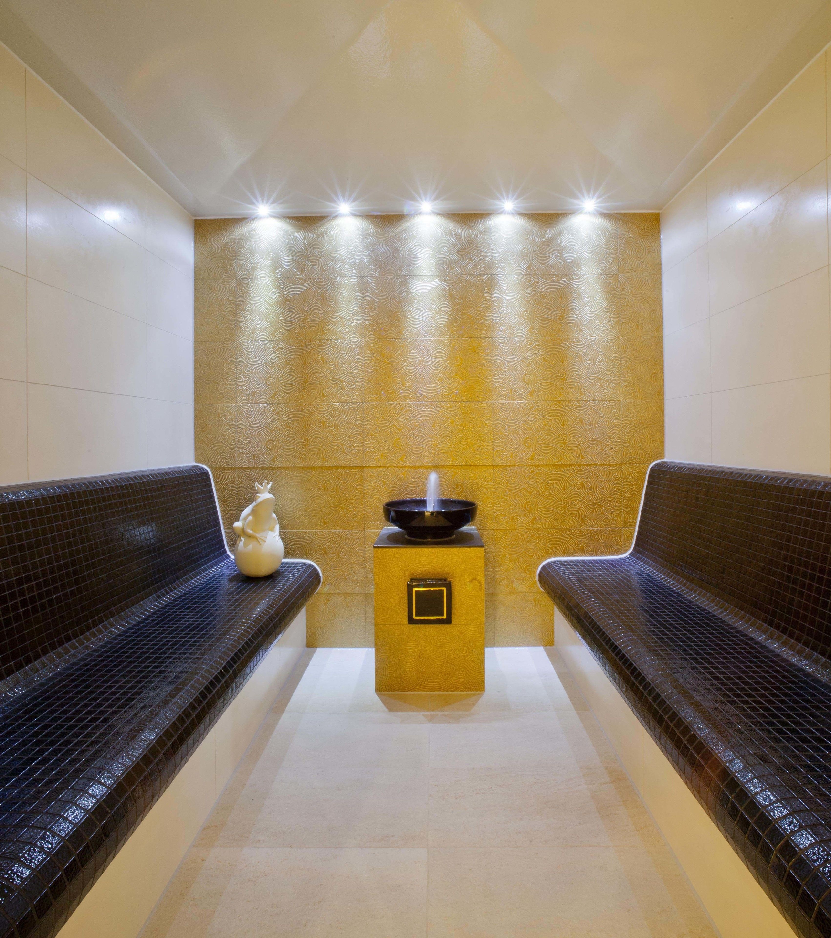 Um espaço de spa com dois bancos marrons escuros, uma pequena estátua branca e uma tigela preta sobre um pedestal.