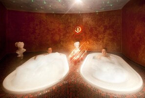 Duas banheiras de hidromassagem em um ambiente com parede texturizada e luminária circular.