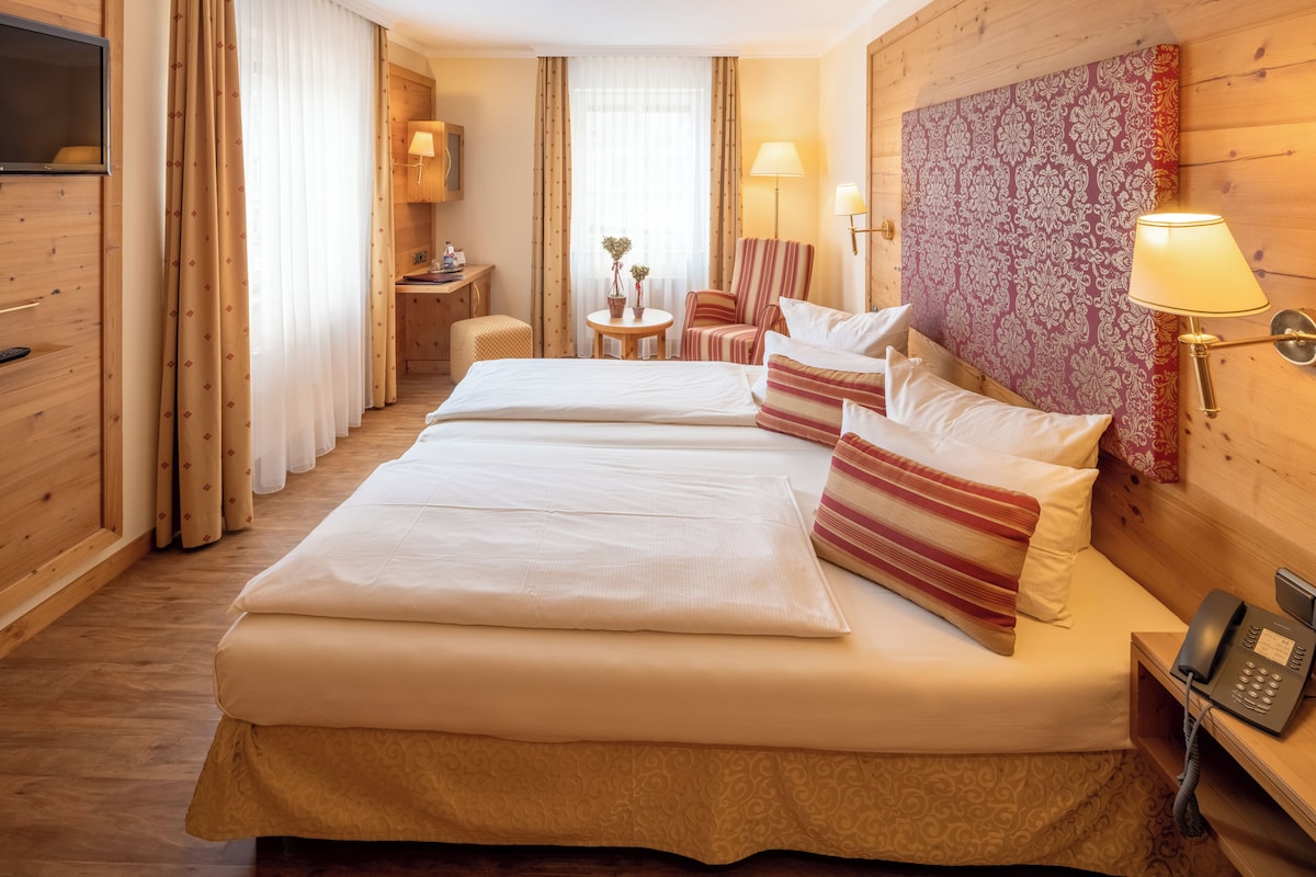 Quarto de hotel com uma cama grande, uma escrivaninha, uma cadeira, um abajur e um telefone.